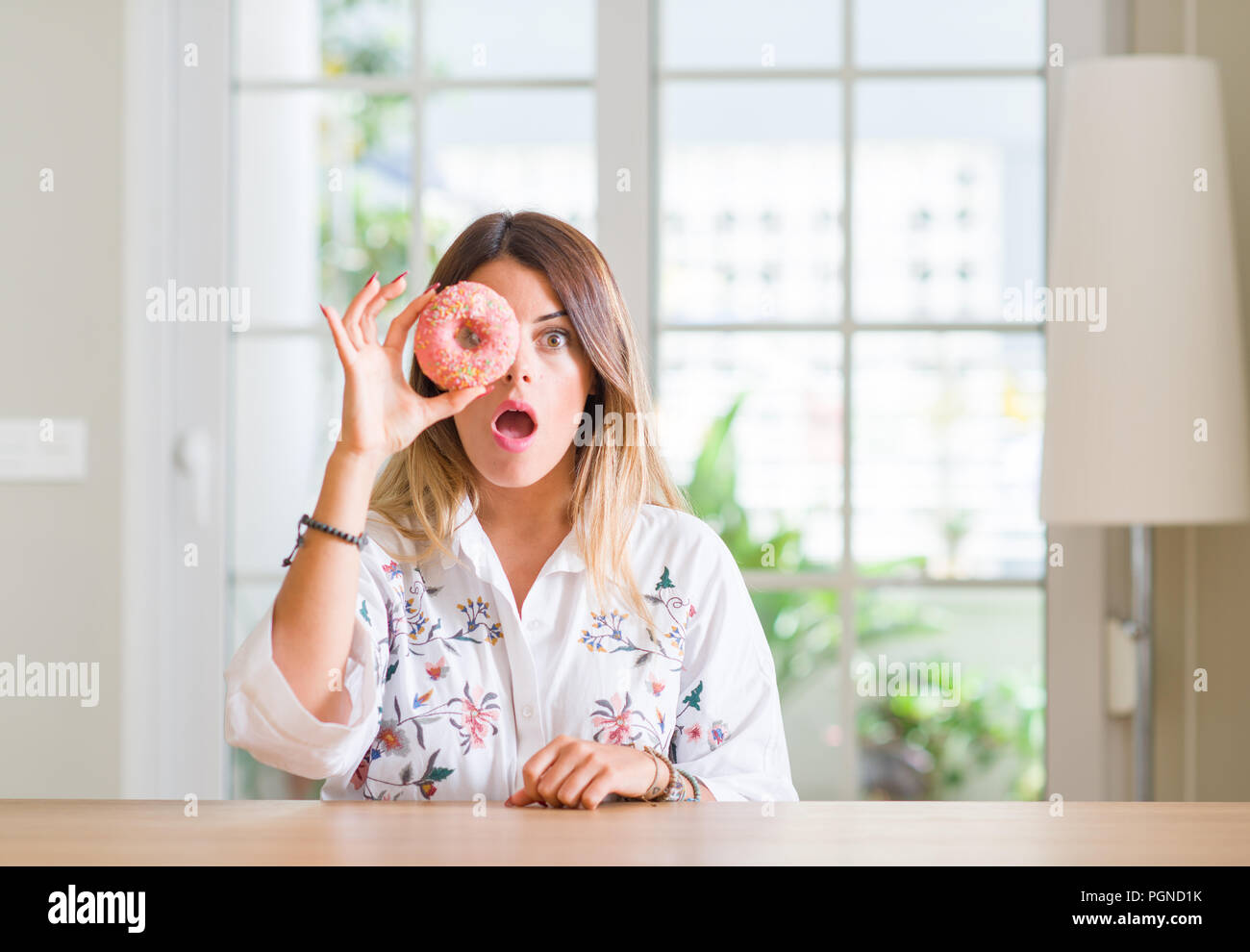 Young woman at home eating a doughnut scared in shock with a surprise ...
