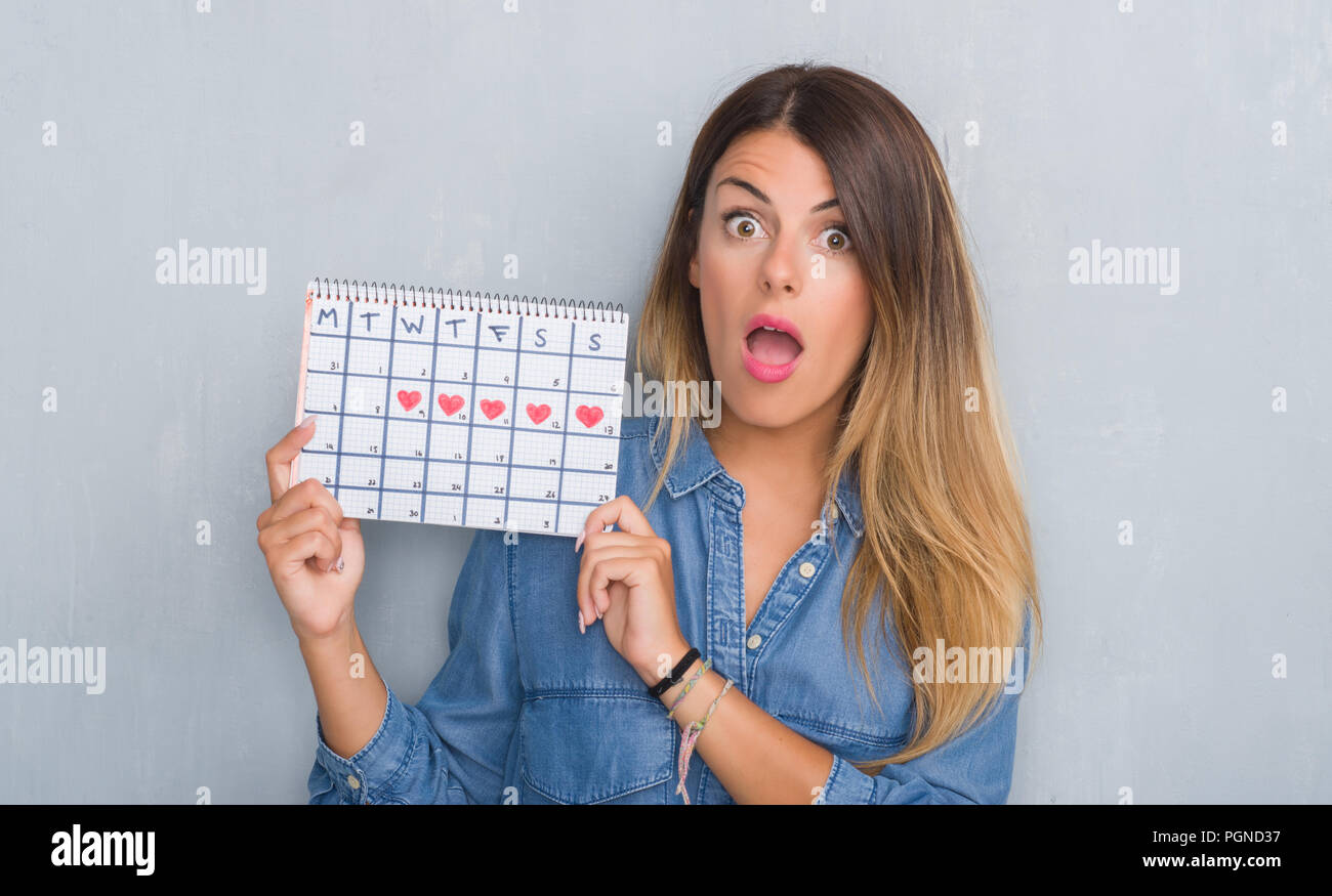 Young adult woman over grey grunge wall showing period calendar scared ...