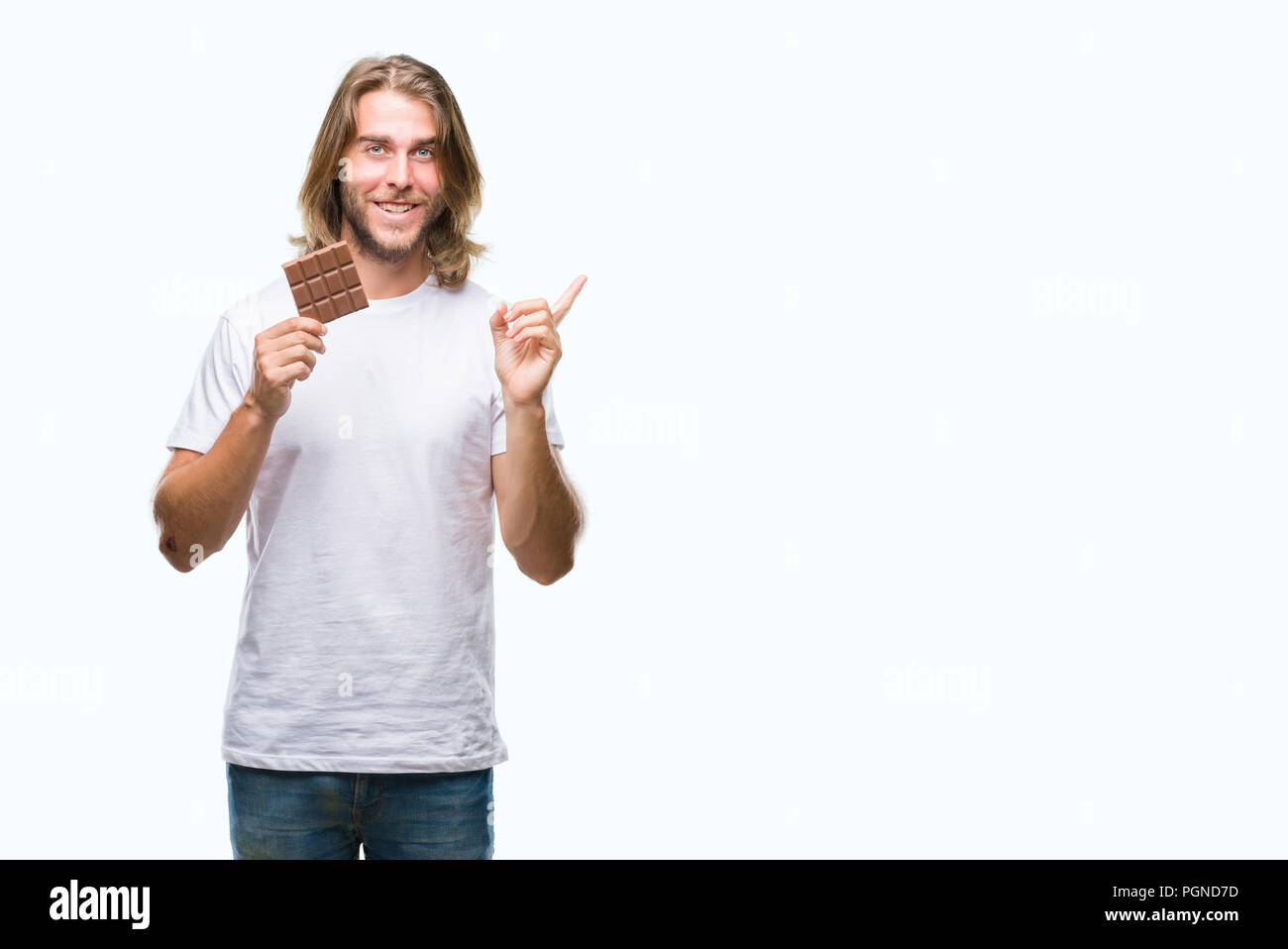 Young handsome man with long hair eating chocolate bar over isolated ...