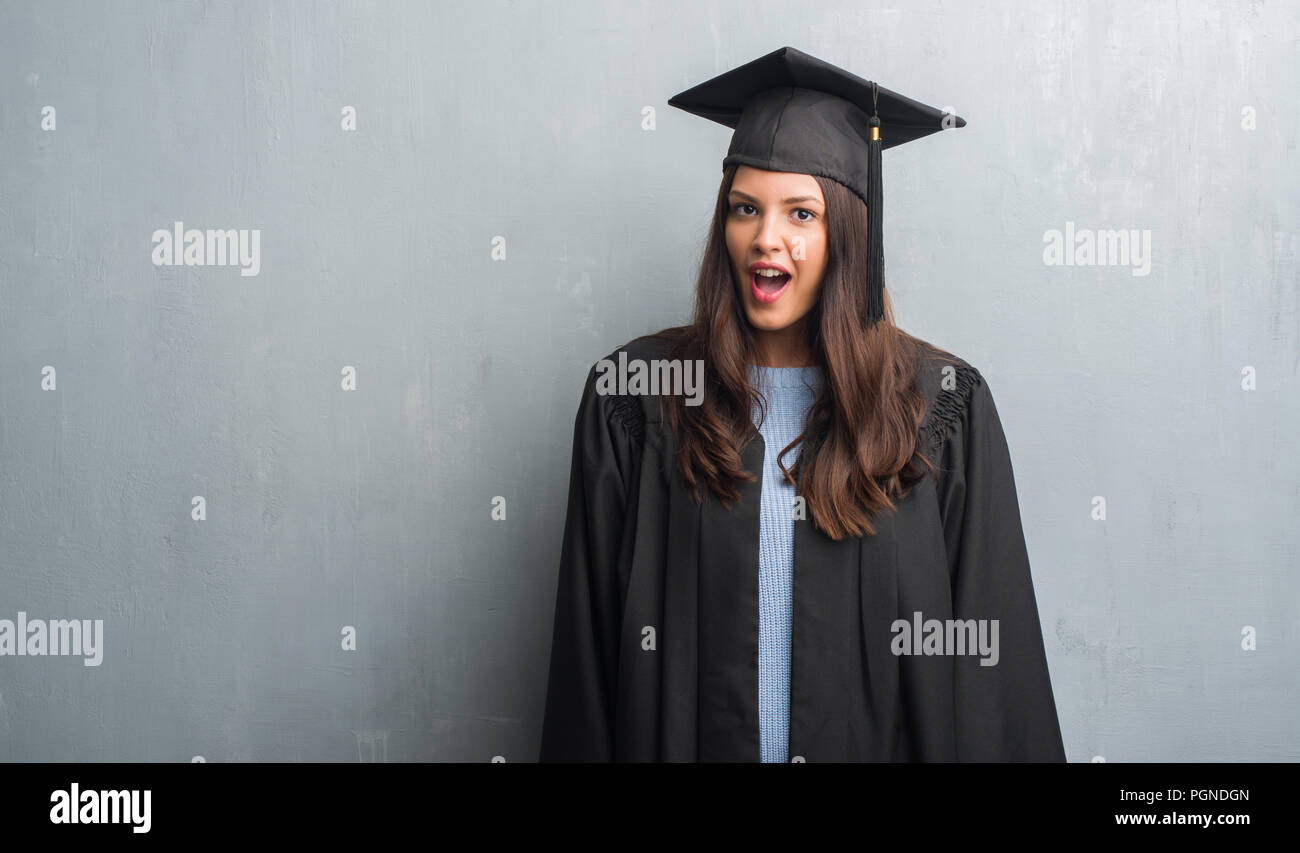 Young brunette woman over grunge grey wall wearing graduate uniform ...