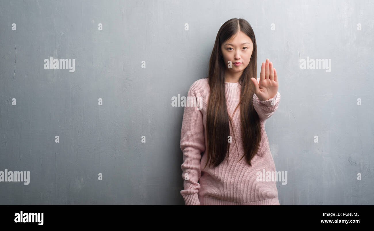 Young Chinese woman over grey wall doing stop sing with palm of the ...