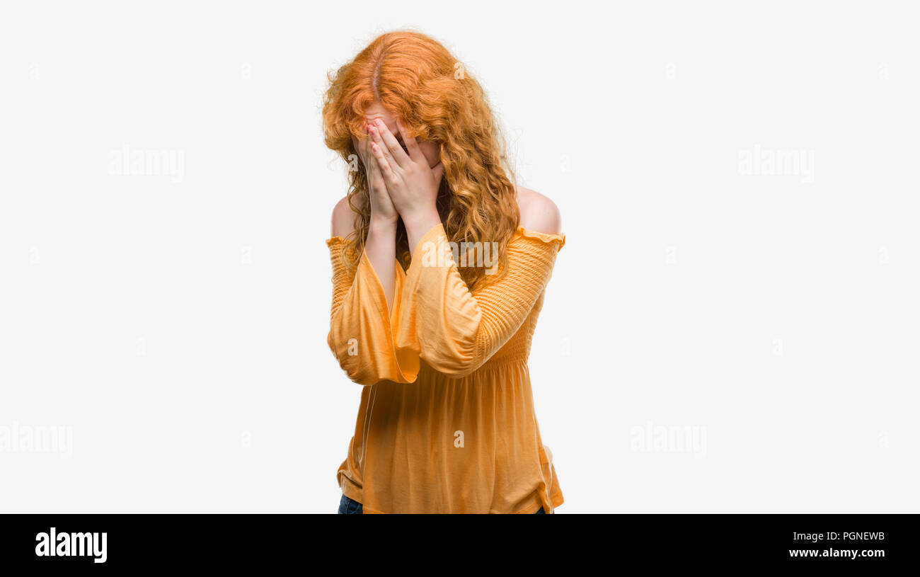 Young redhead woman with sad expression covering face with hands while ...