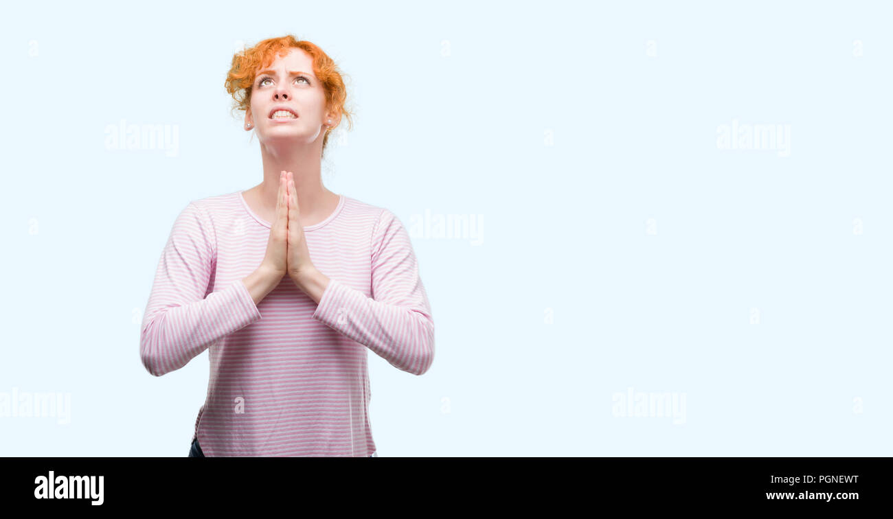 Young redhead woman begging and praying with hands together with hope ...