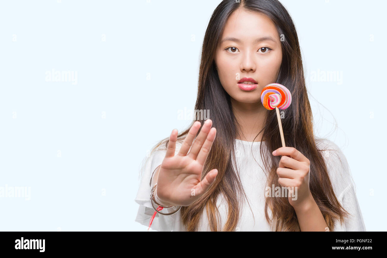 Young asian woman eating lollipop candy over isolated background with ...
