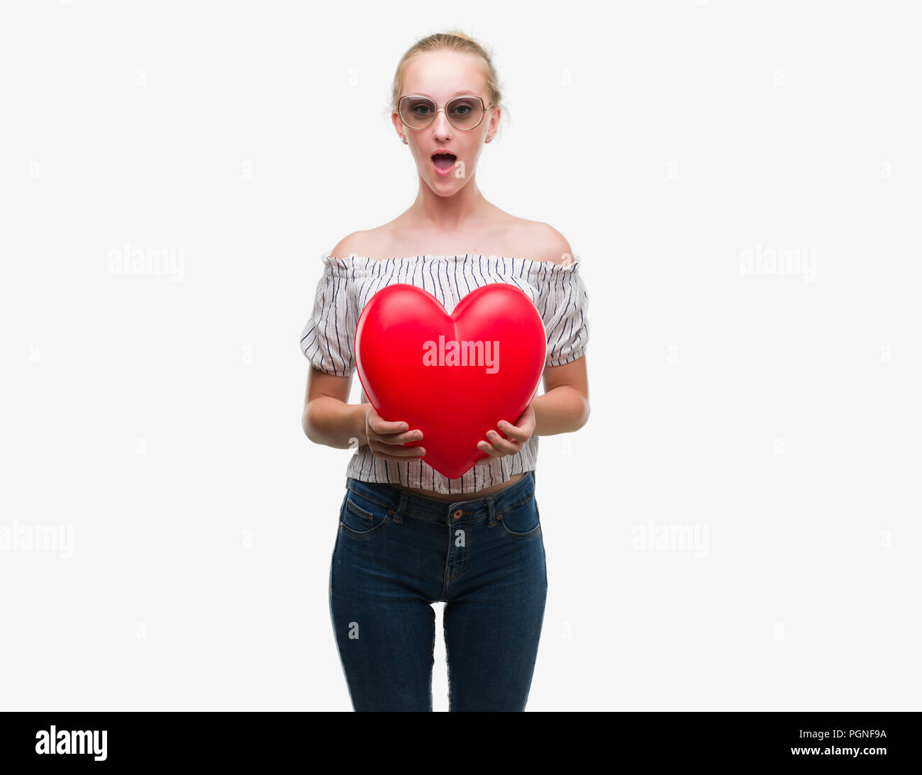 Blonde teenager woman holding red heart scared in shock with a surprise ...