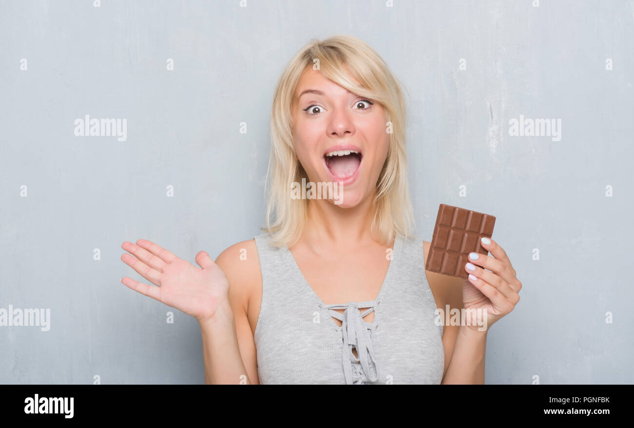 Caucasian adult woman over grey grunge wall eating chocolate bar very ...