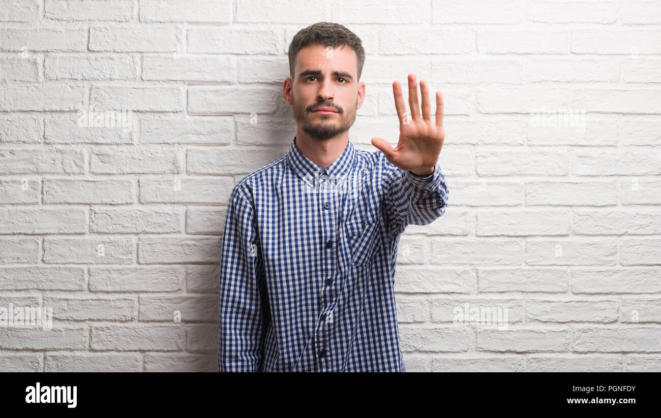 Young adult man standing over white brick wall with open hand doing ...