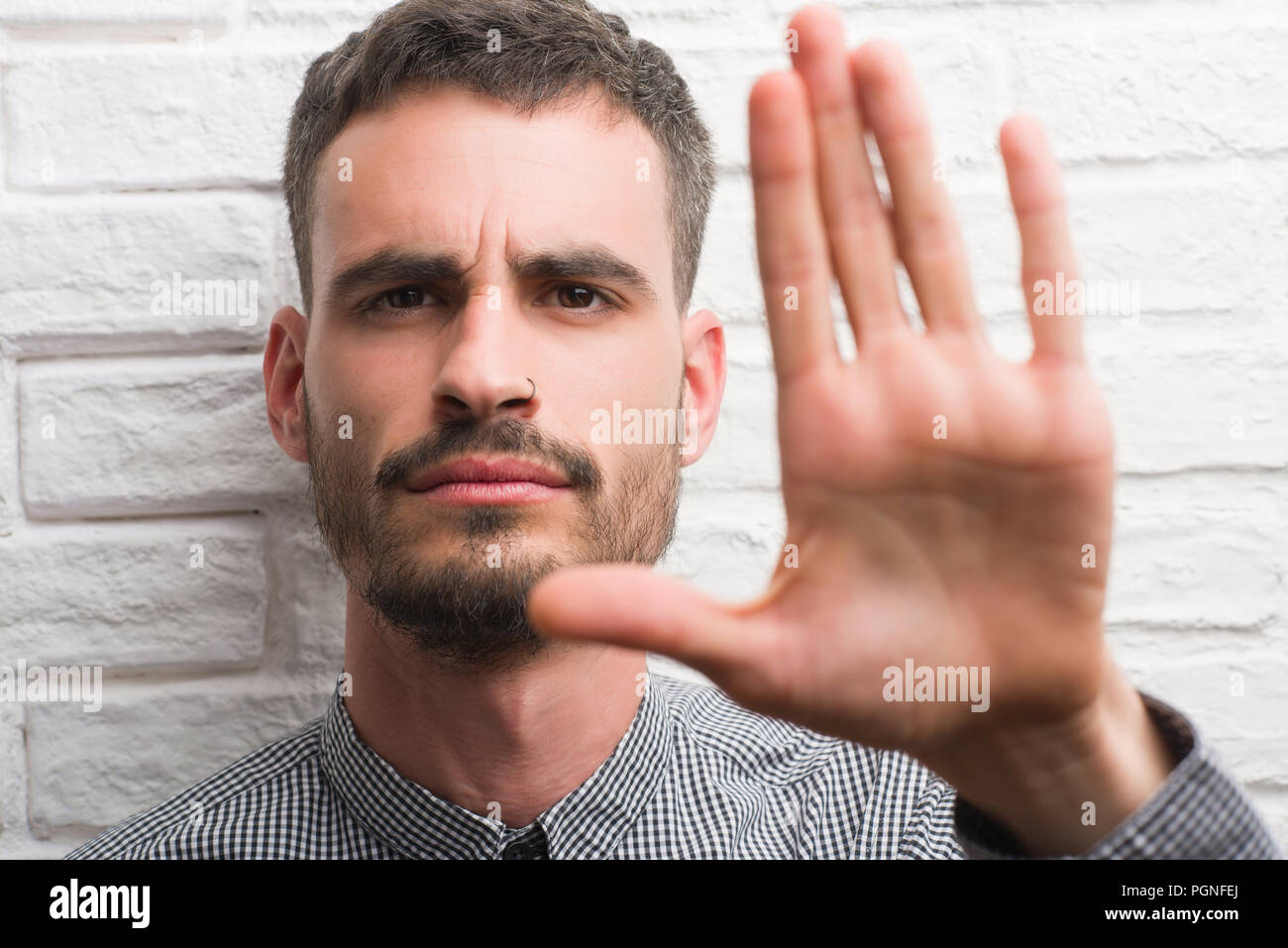 Young adult man standing over white brick wall with open hand doing ...