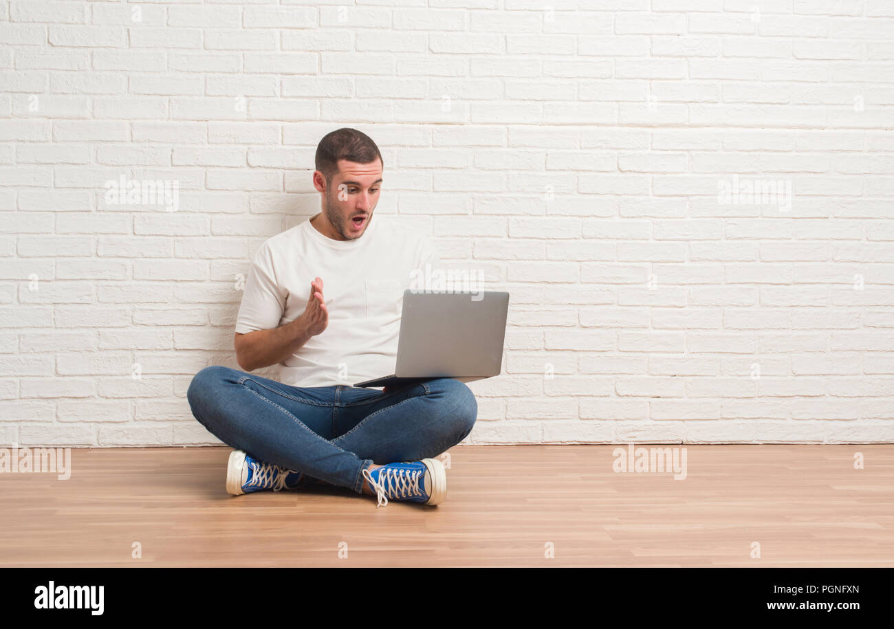 Young caucasian man sitting over white brick wall using computer laptop ...