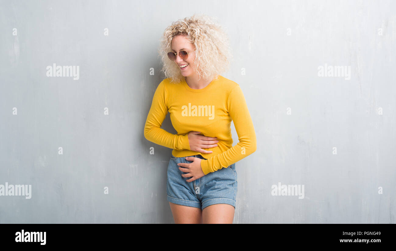 Young blonde woman with curly hair over grunge grey background with ...