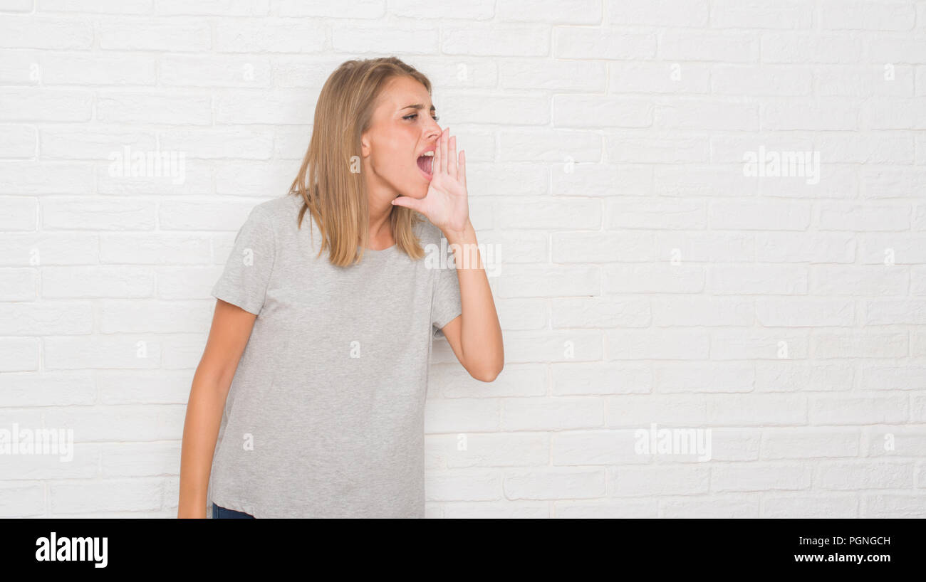 Beautiful young woman over white brick wall shouting and screaming loud ...
