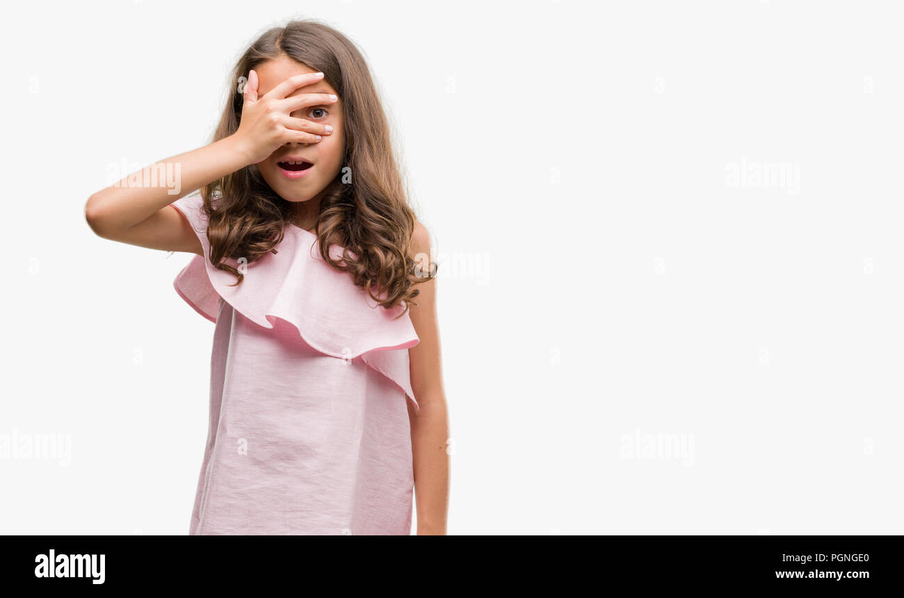 Brunette hispanic girl wearing pink dress peeking in shock covering ...