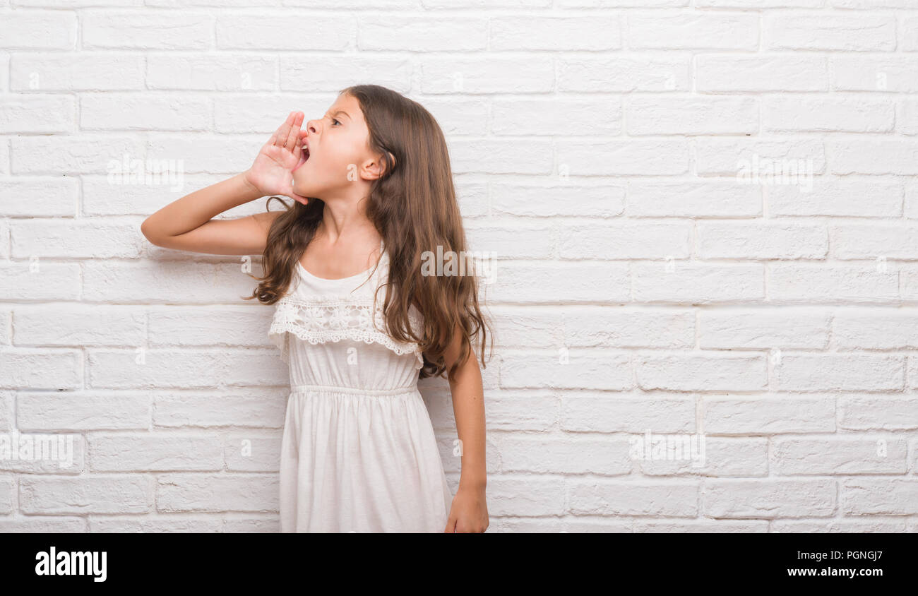 Young hispanic kid over white brick wall shouting and screaming loud to ...