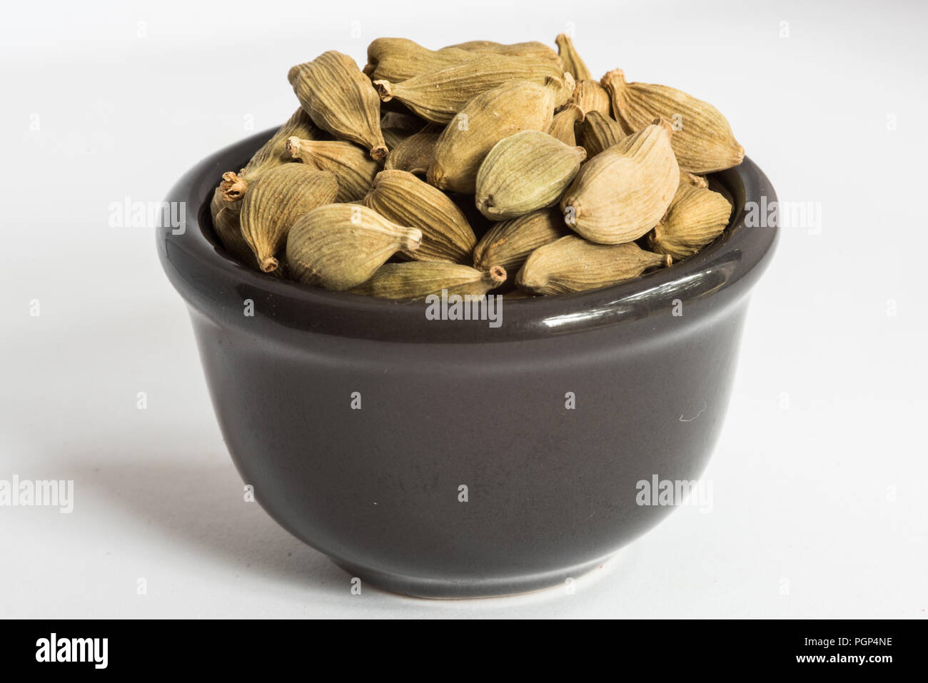 Cardamom pods in a grey cup shown on a white background Stock Photo - Alamy