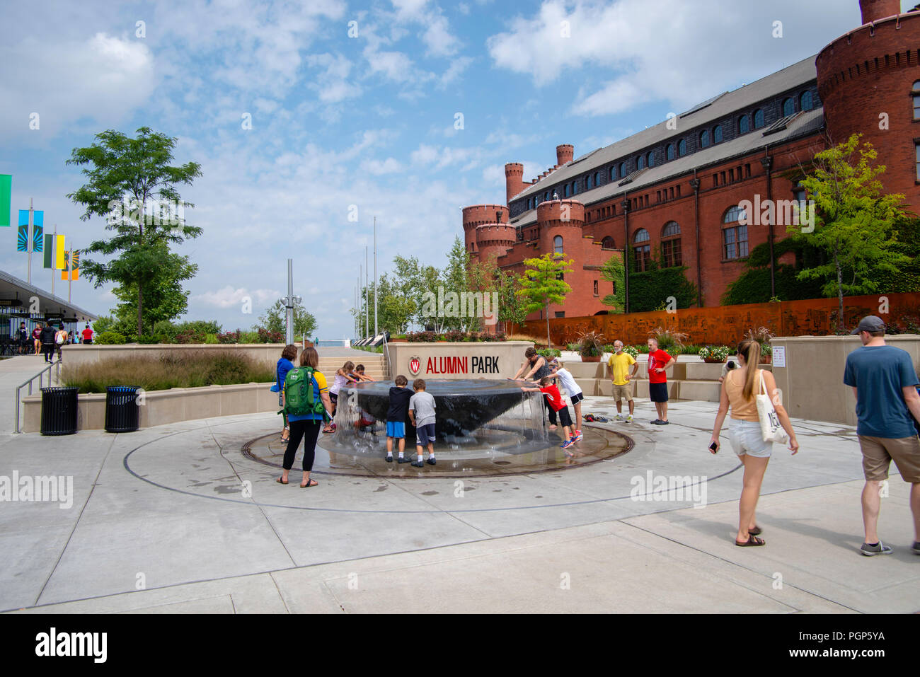 Children and adults enjoy the water fountain at Alumni Park, University ...