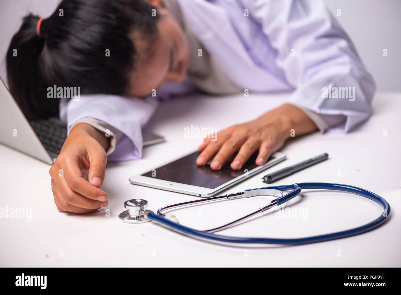 Young female doctor sleeping at her desk working over laptop and report ...