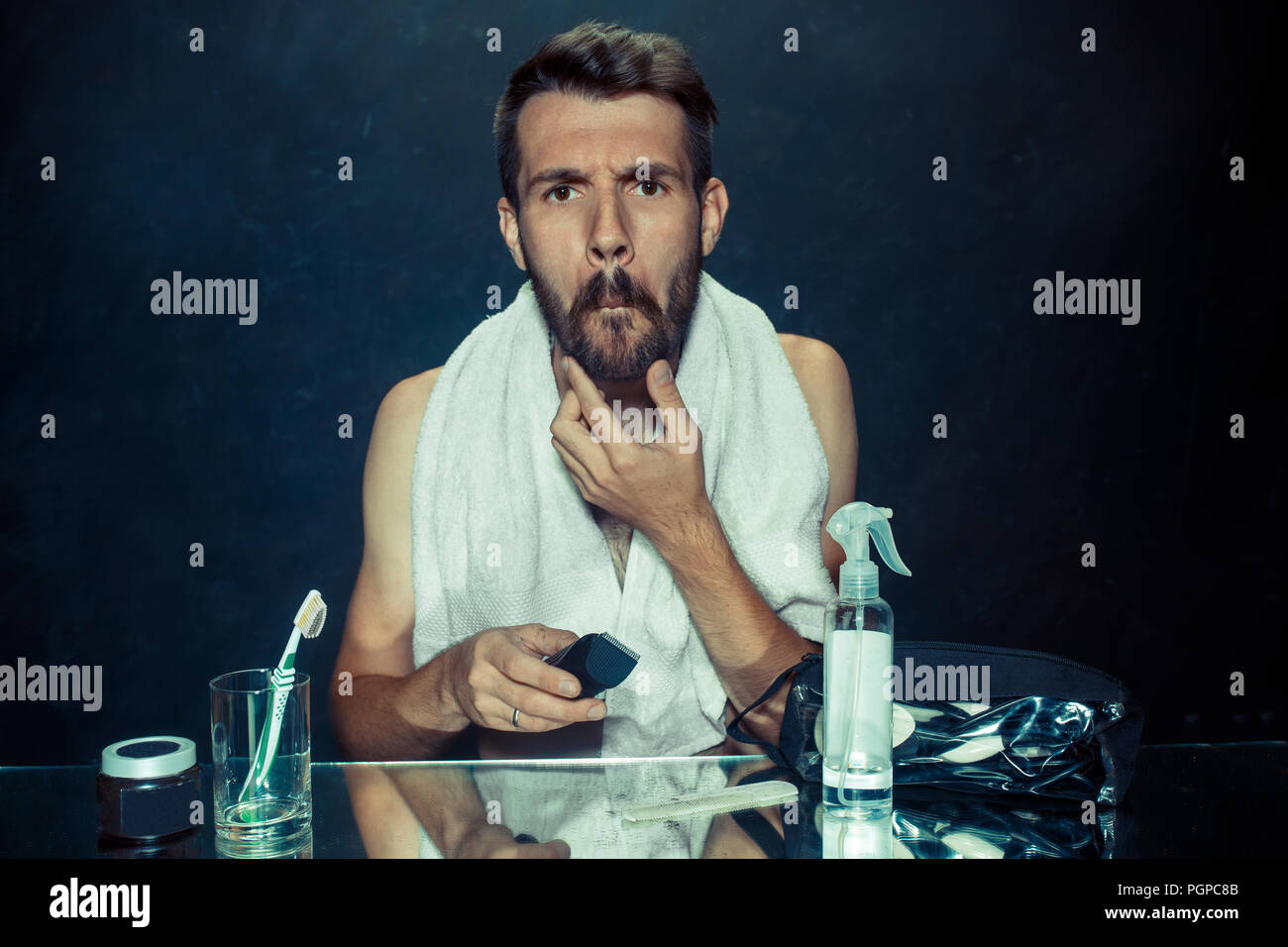 The young man in bedroom sitting in front of the mirror scratching his ...