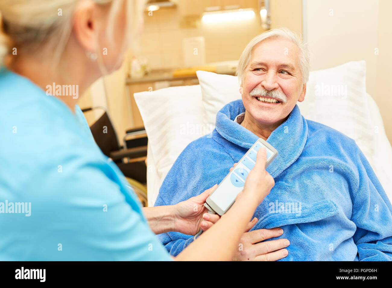 Caregiver with remote control on nursing bed by senior in retirement ...