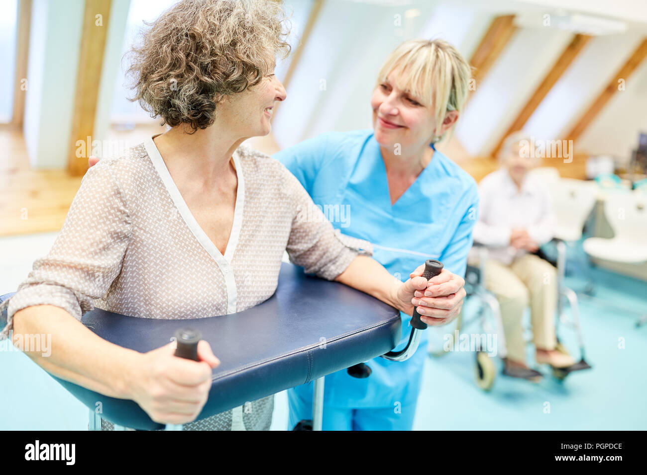 Senior woman with walker in physiotherapy is assisted by therapist ...