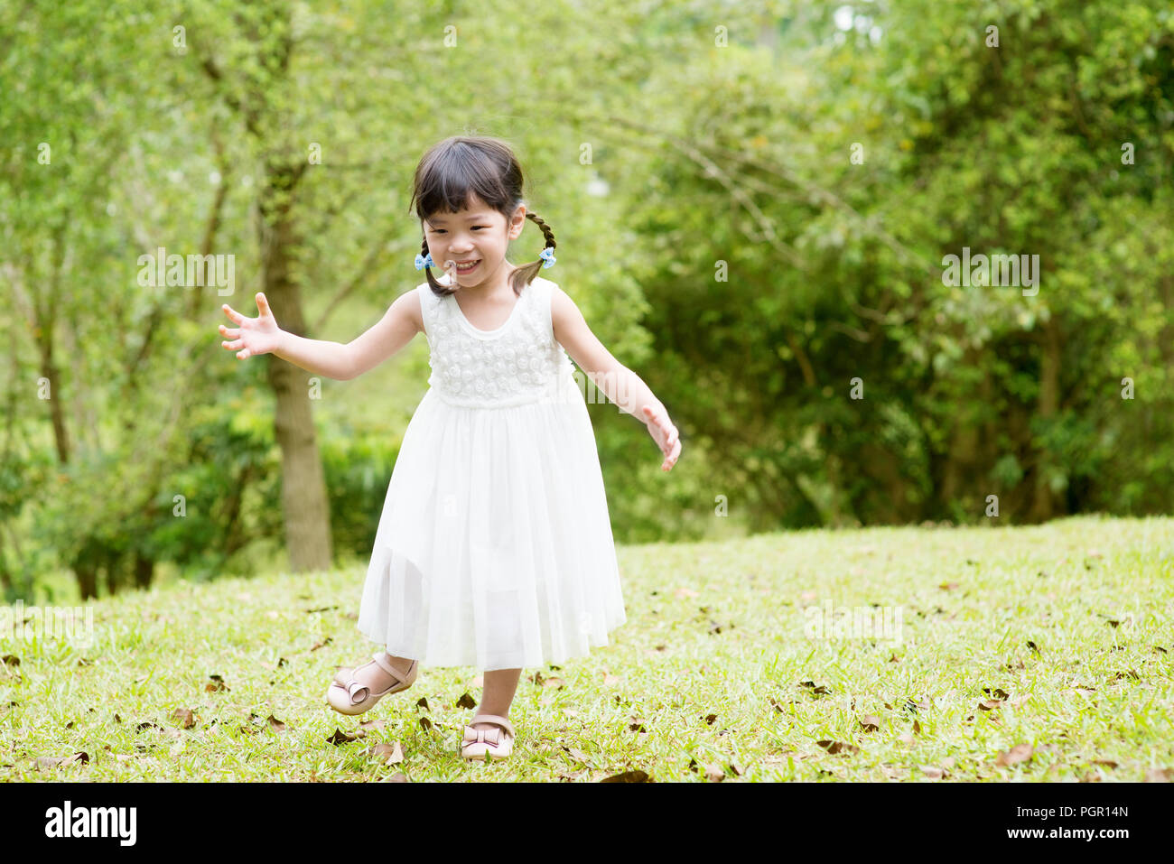 Happy little girl running at green park. Asian family outdoors portrait ...