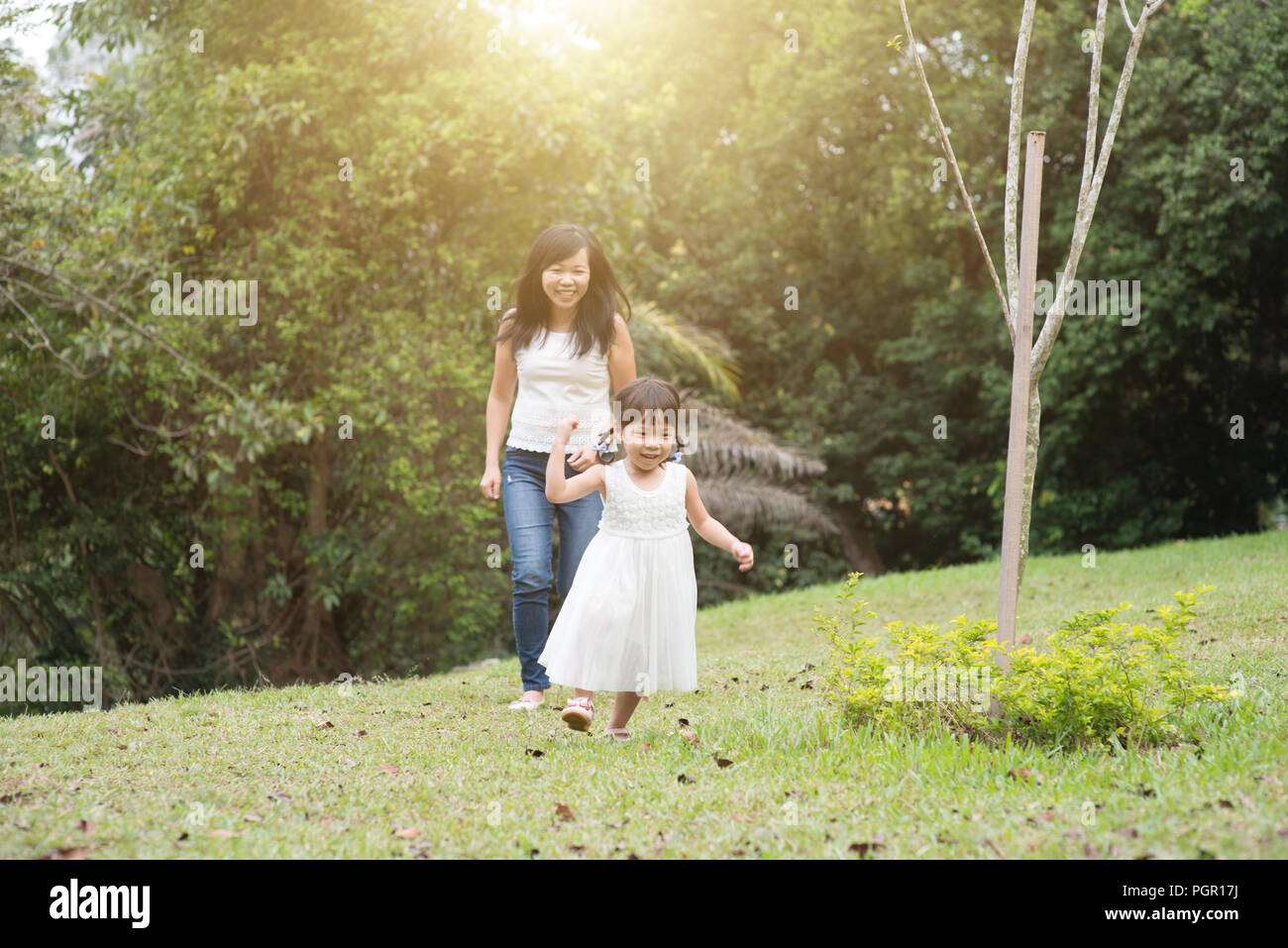 Mother and little girl play chasing at green park. Asian family ...