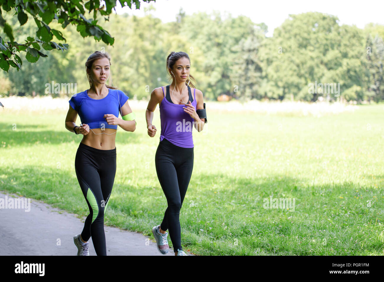 Two beautiful and attractive fitness girls are jogging in the park on a ...