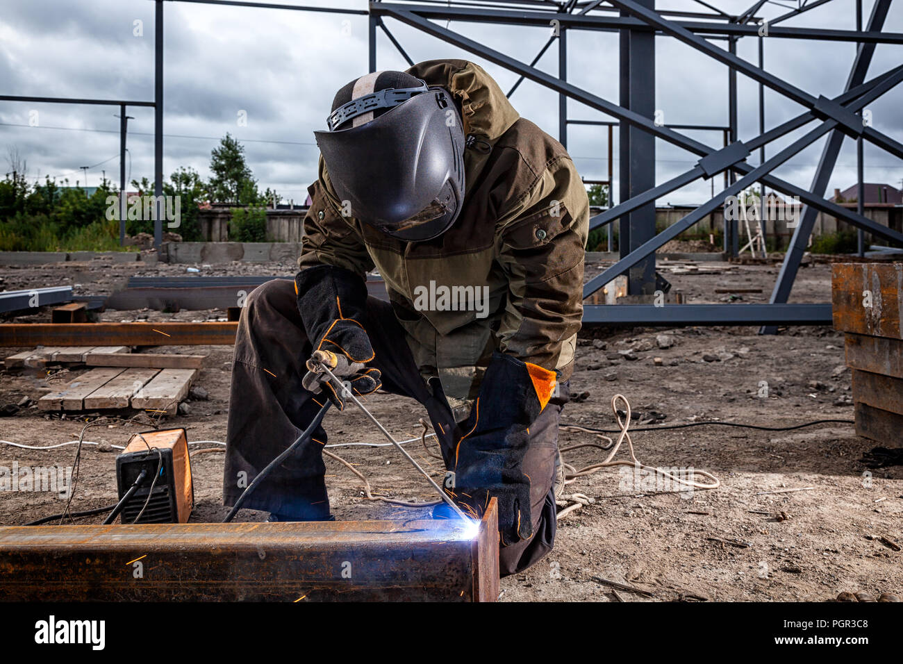 Man welder in welding mask, building uniform and blue protective gloves ...