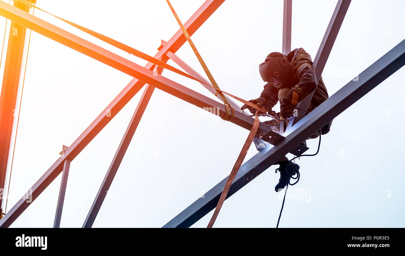 A man welder working at height with insurance in welding mask is weld ...