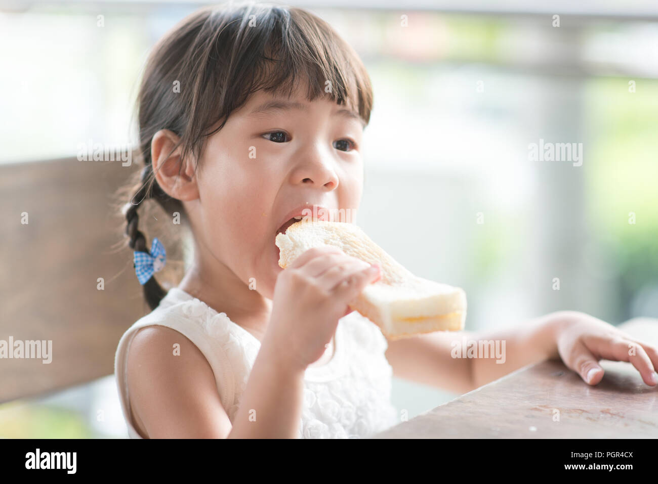 Asian child eating butter toast at cafe. Outdoor family lifestyle with ...