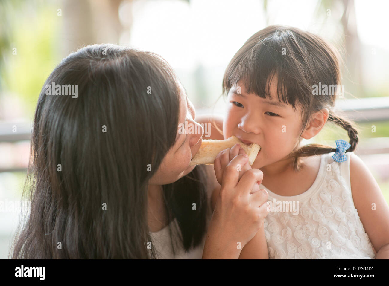 Cute Asian child eating and sharing butter toast with mom at cafe ...