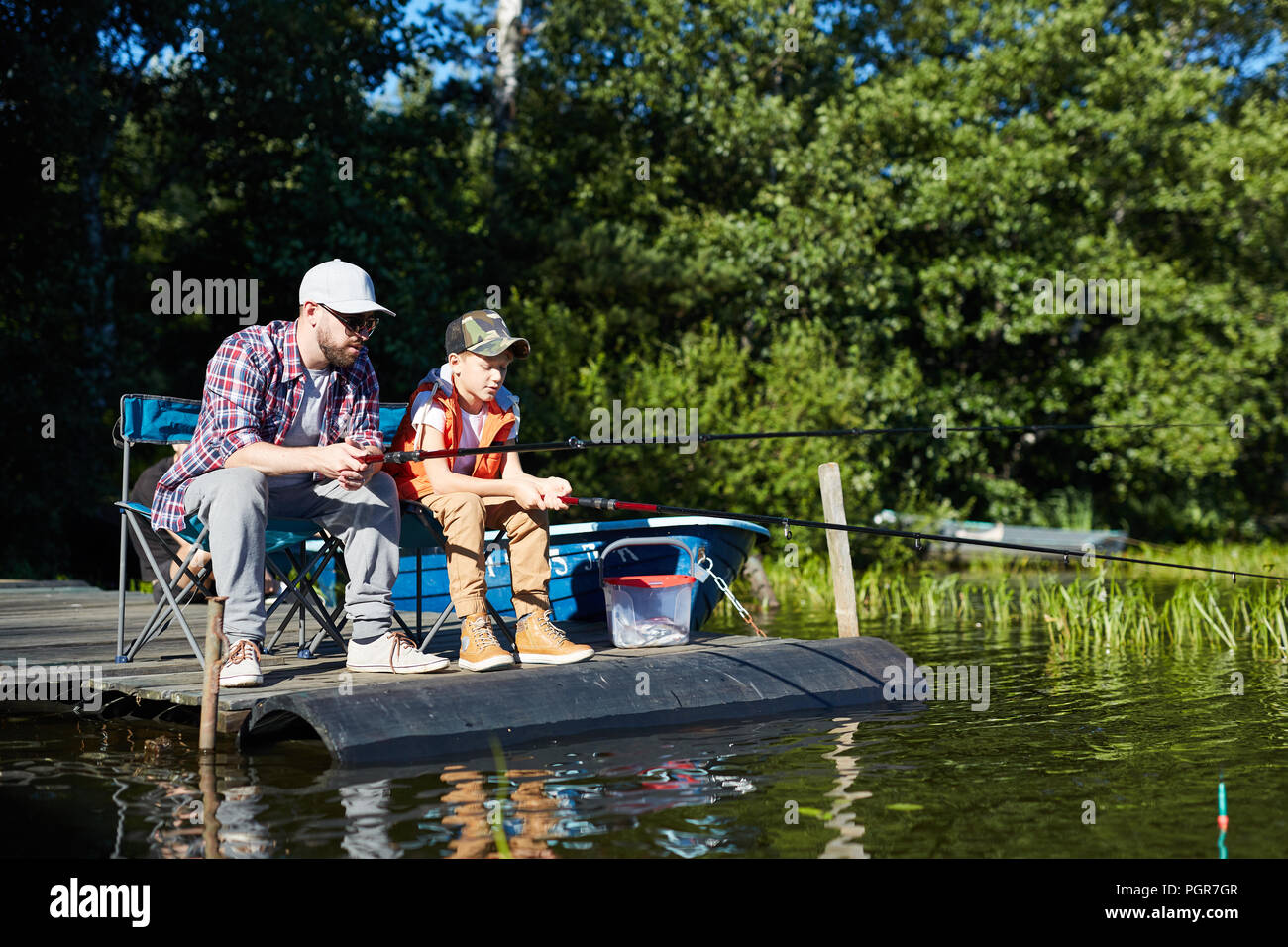 Dad and son fishing at lake in the countryside, they sitting with ...