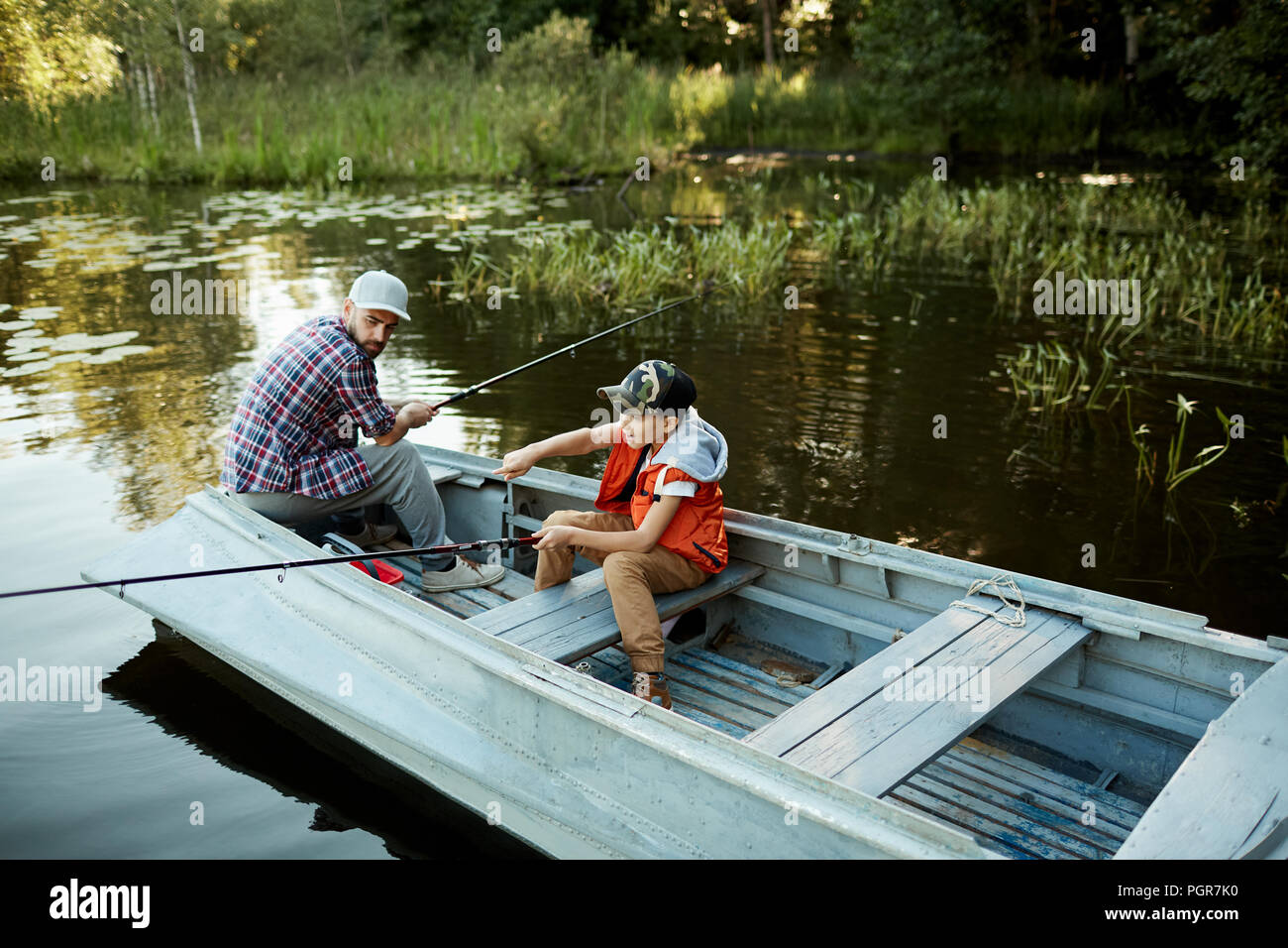 Dad and son sitting in boat and fishing on lake, the boy showing his ...