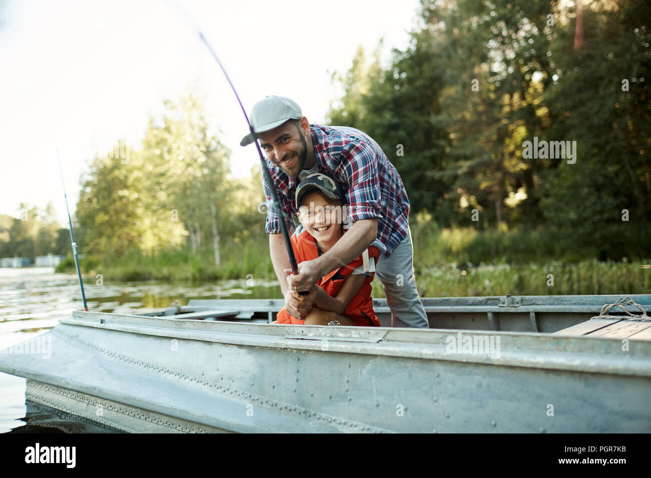 Father teaching his happy son to fishing, he helps him to hold a rod ...