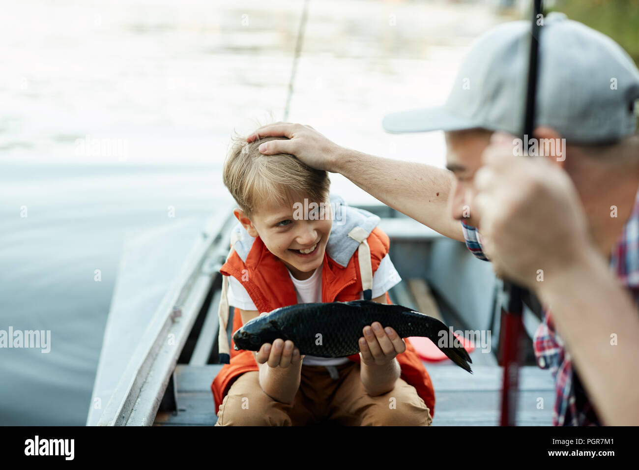 Happy boy holding big fish, and showing it to his father, while they ...