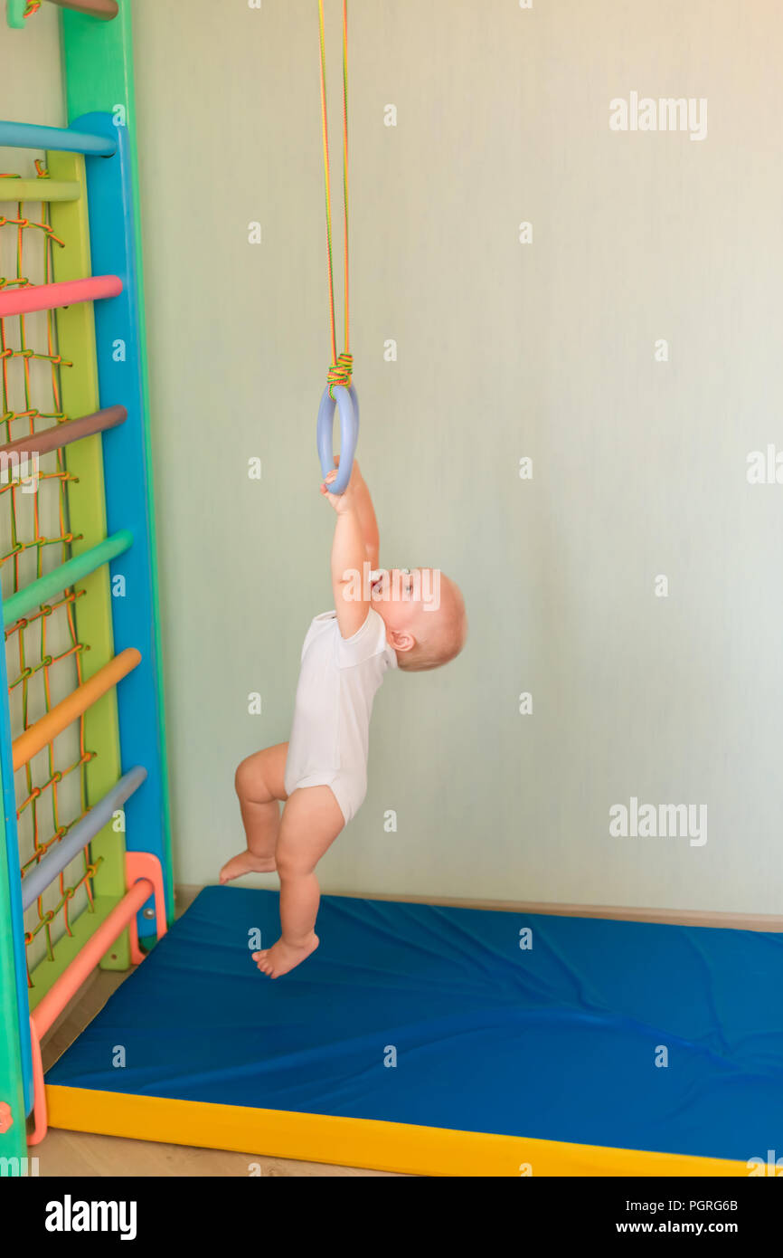 Cute baby boy hanging on rings on home wall gym. Baby early sportive ...