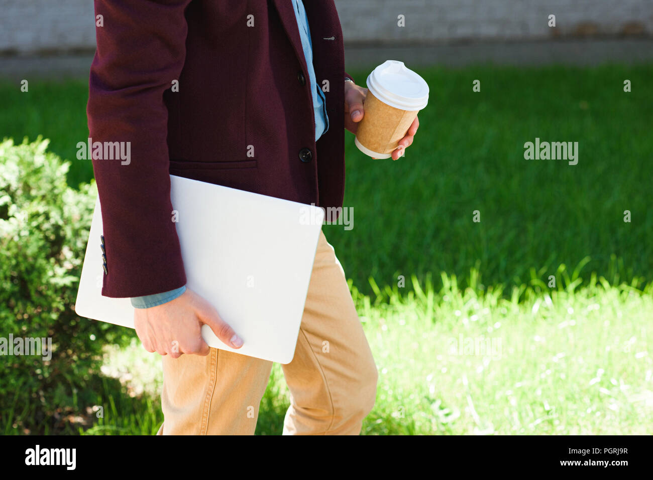 cropped shot of man with laptop and paper cup walking outside Stock ...