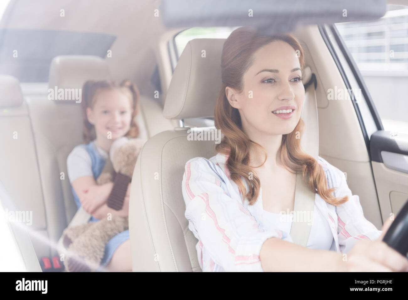 selective focus of smiling mother driving car with daughter on ...
