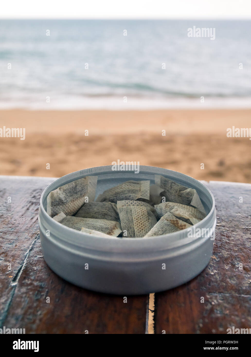 Swedish snus tobaco on a wood table in Thailand. Beach in background ...
