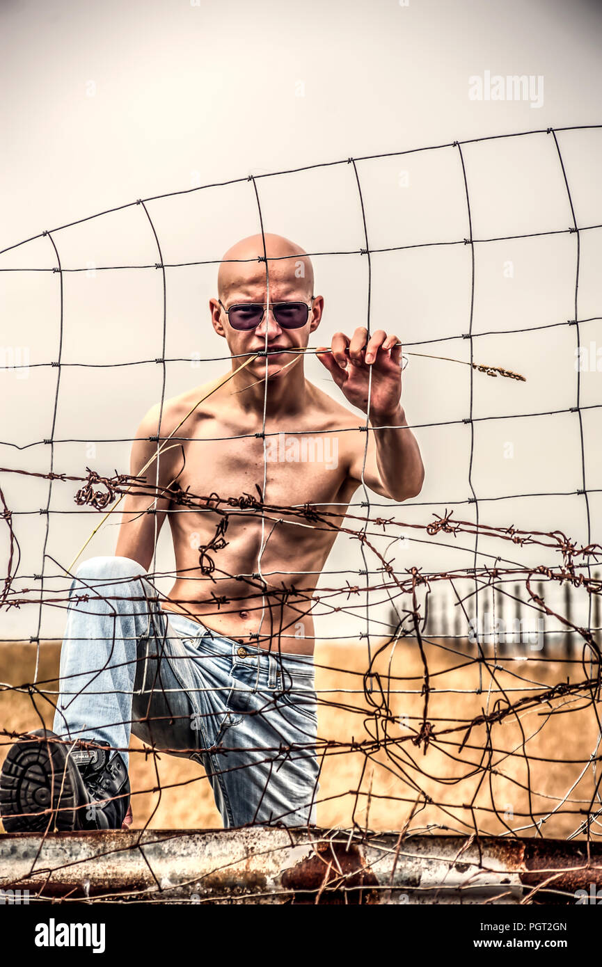 young angry man with bald head standing near wire fence Stock Photo - Alamy