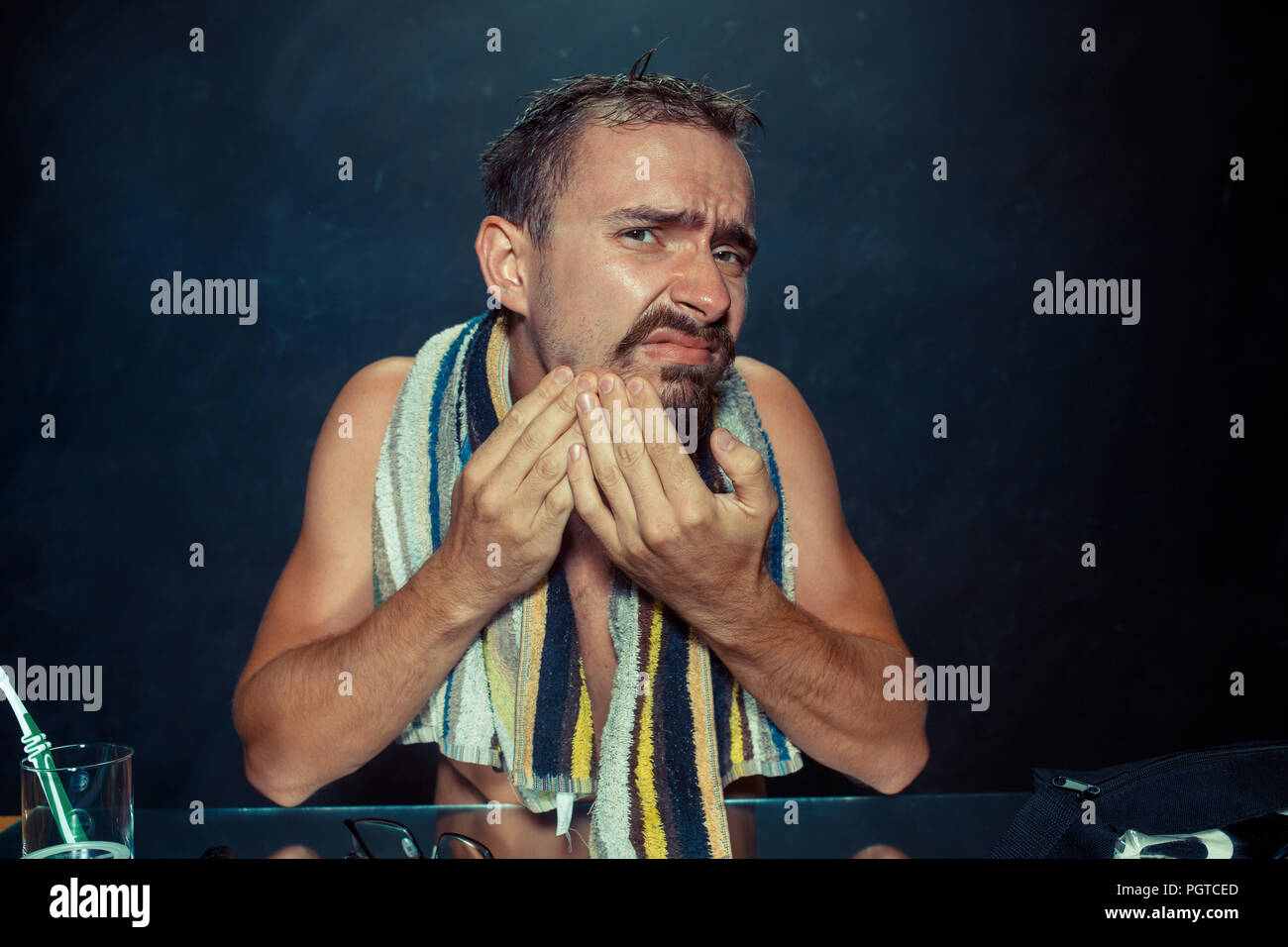 The young man in bedroom sitting in front of the mirror scratching his ...