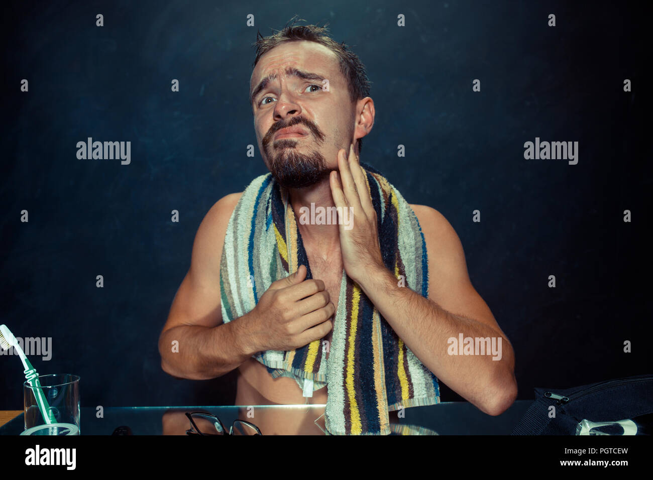 The young man in bedroom sitting in front of the mirror scratching his ...
