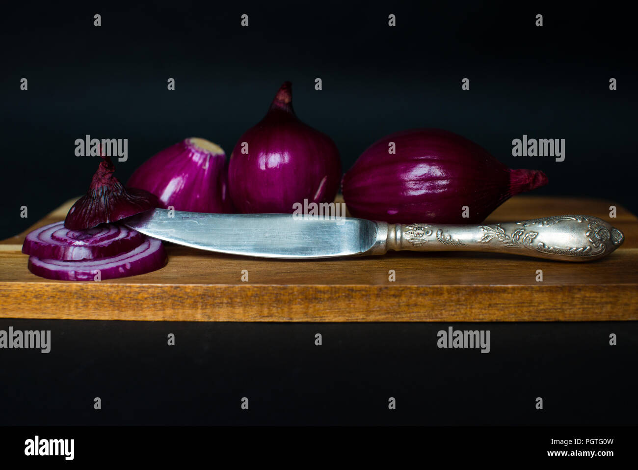 Red sliced onions and a silver kinfe isolated on the black background ...