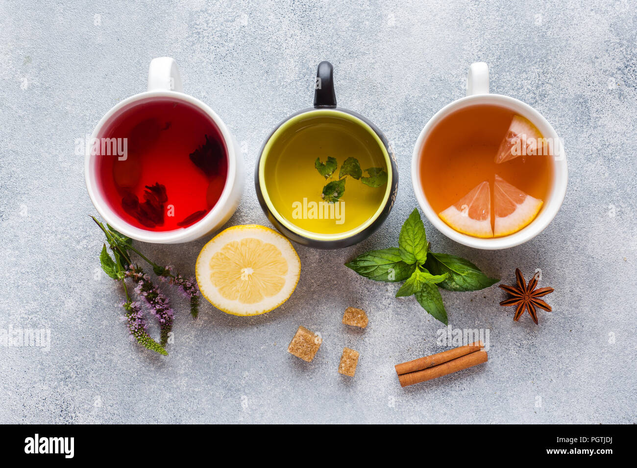 Cups with different tea Red, green and black on grey table. mint and ...