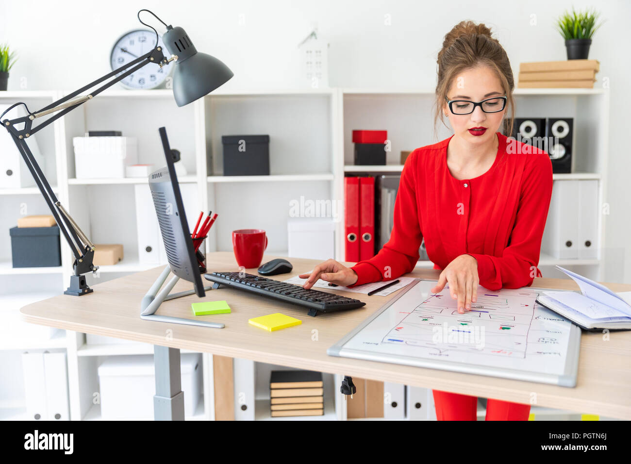 A young girl is sitting at the desk in the office and typing on the ...