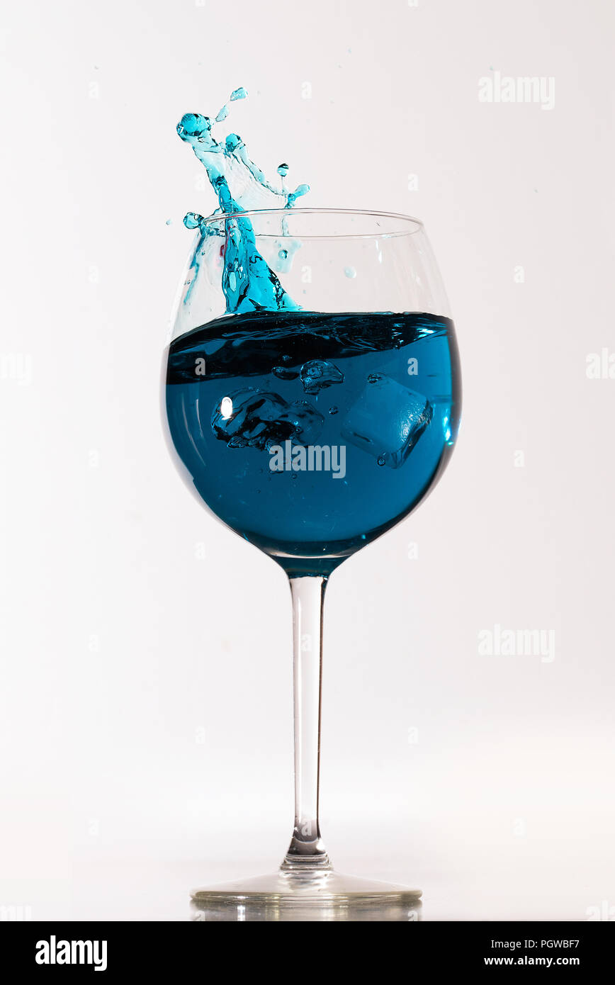 Blue drink in a tall wine glass splashing with ice cube Stock Photo - Alamy