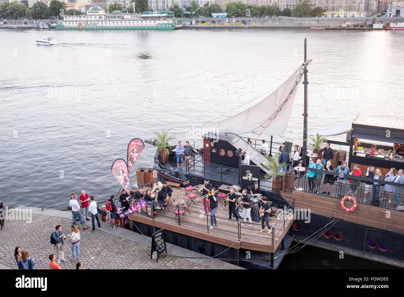 Musicians play on the deck of a barge converted into a bar at dusk on ...