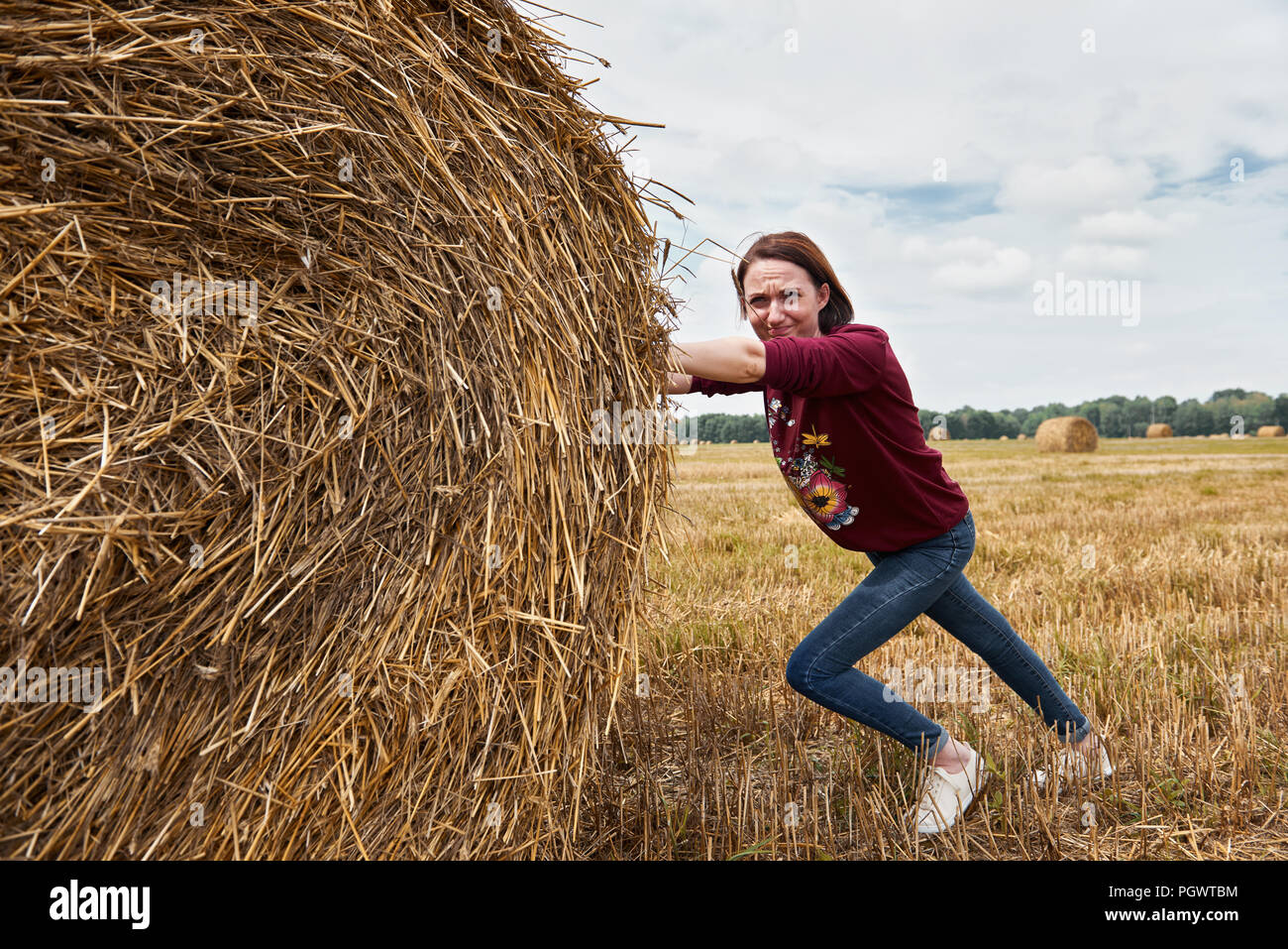young girl having fun in the field, pushes the haystack Stock Photo - Alamy