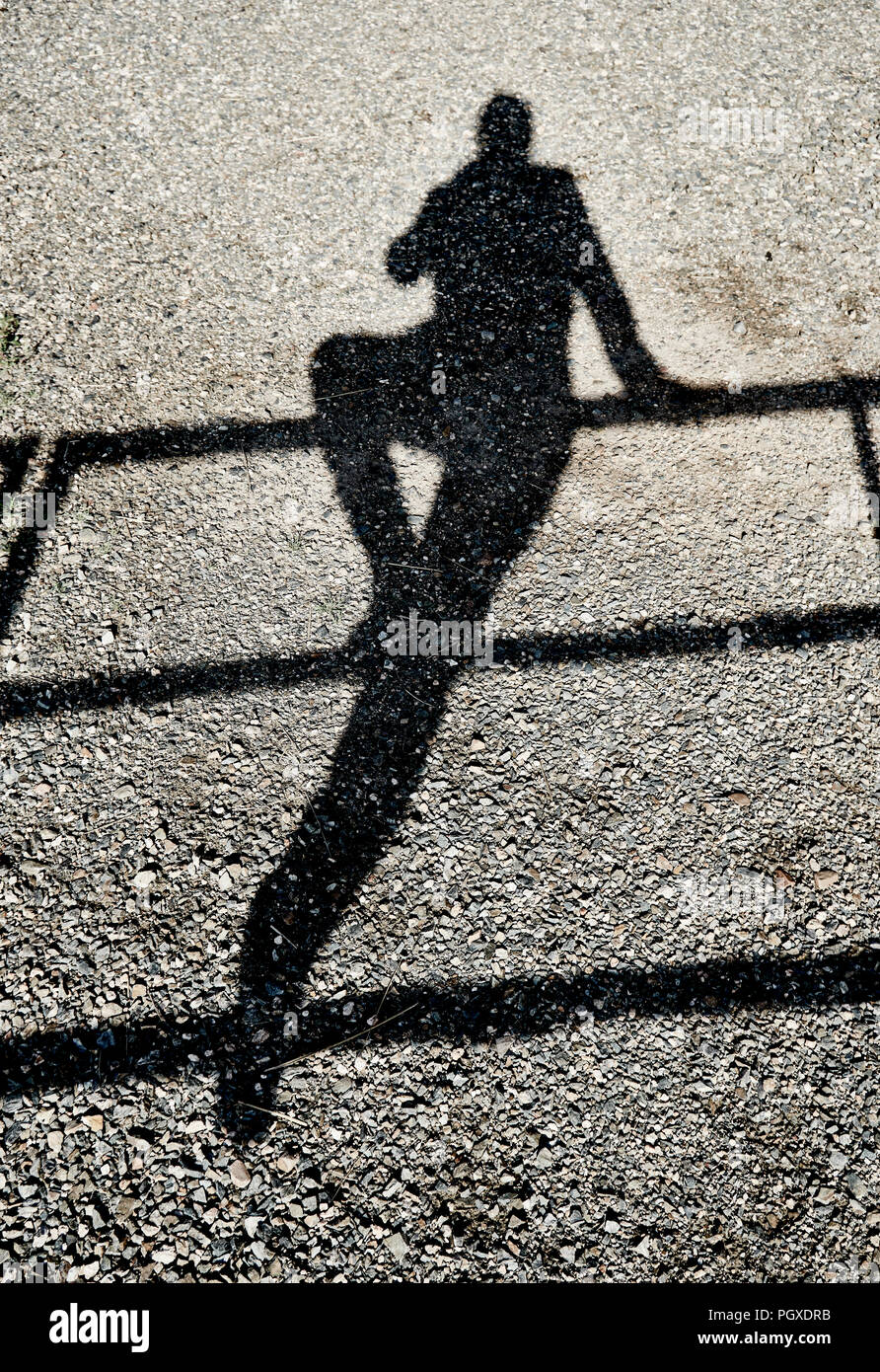 Shadow of a person balancing on one leg on a rail reflected on a gravel ...
