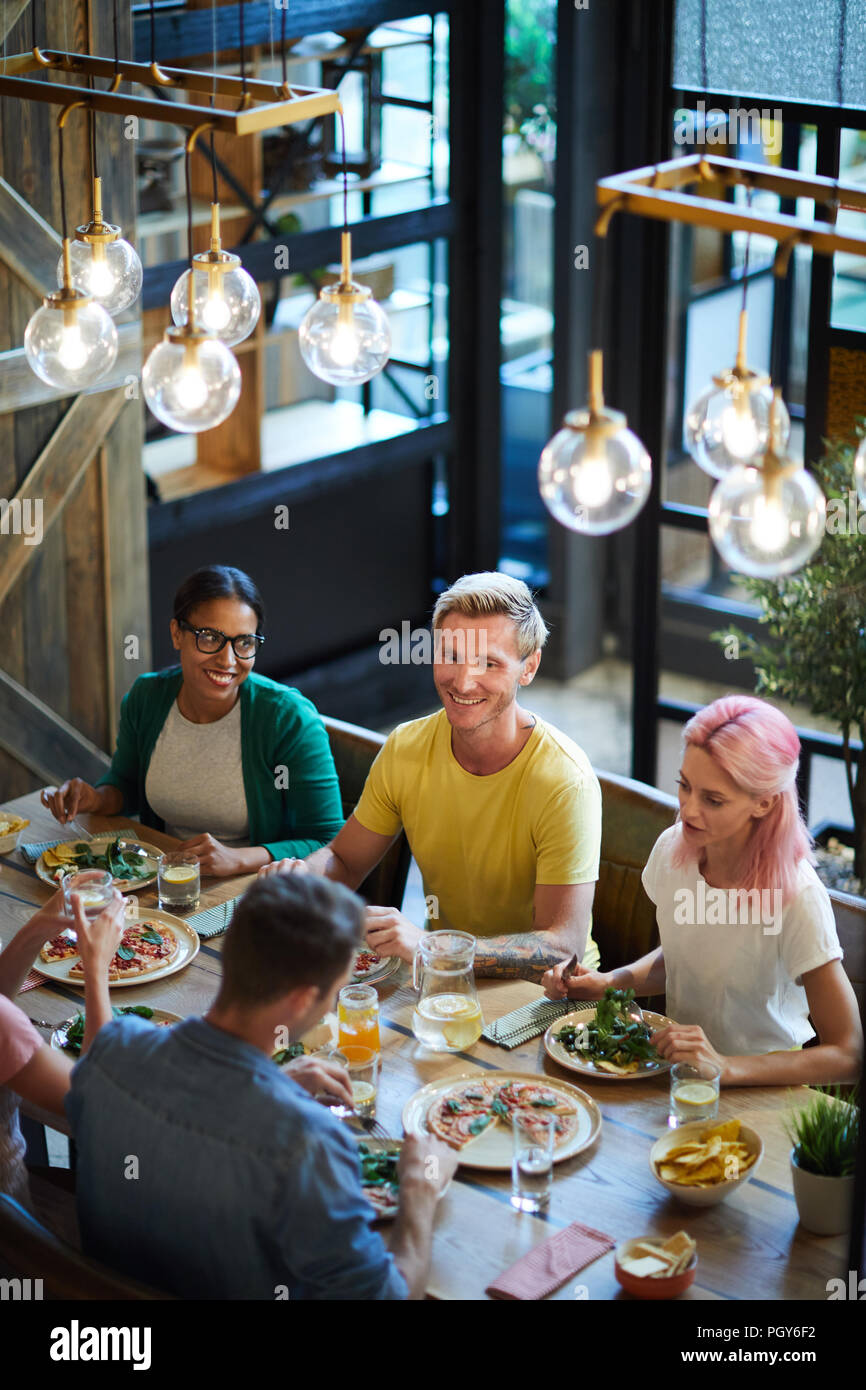 One of guys sitting by served table between two intercultural girls ...