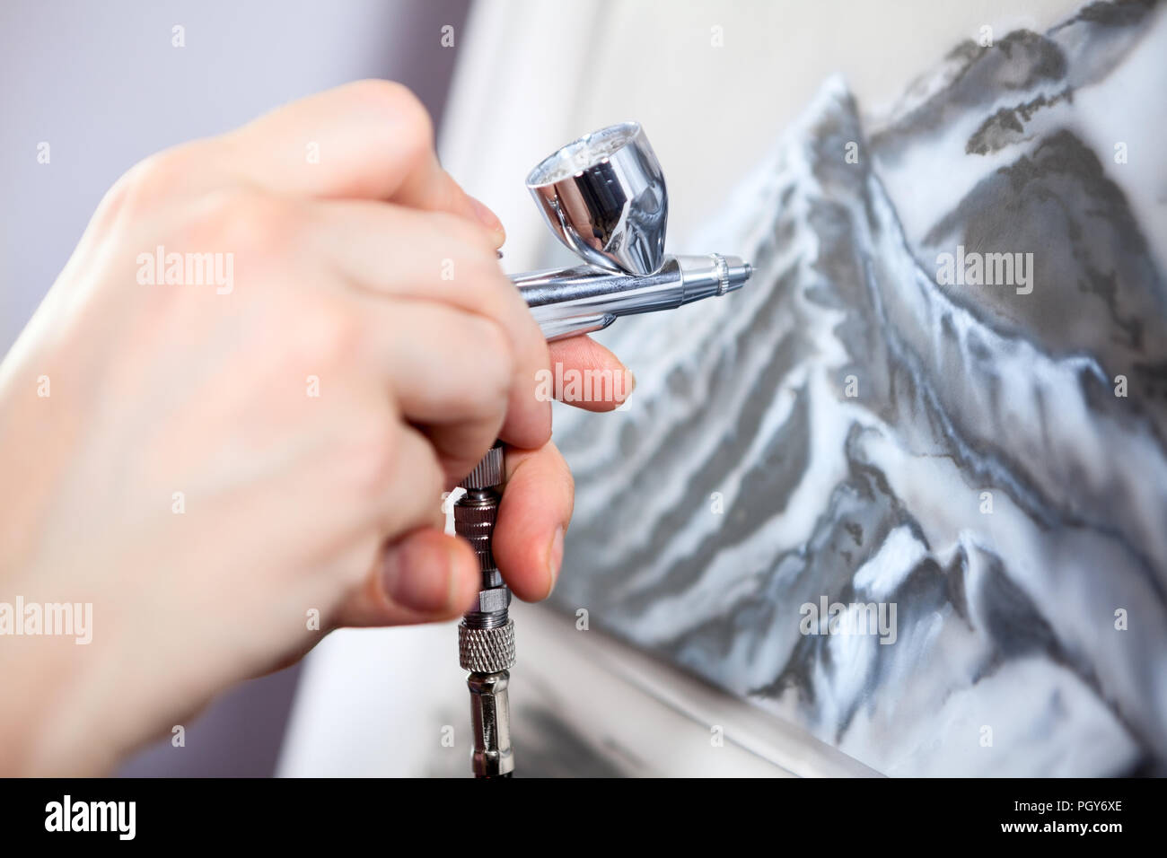An aerograph unit or paint sprayer in human hand drawing on canvas ...